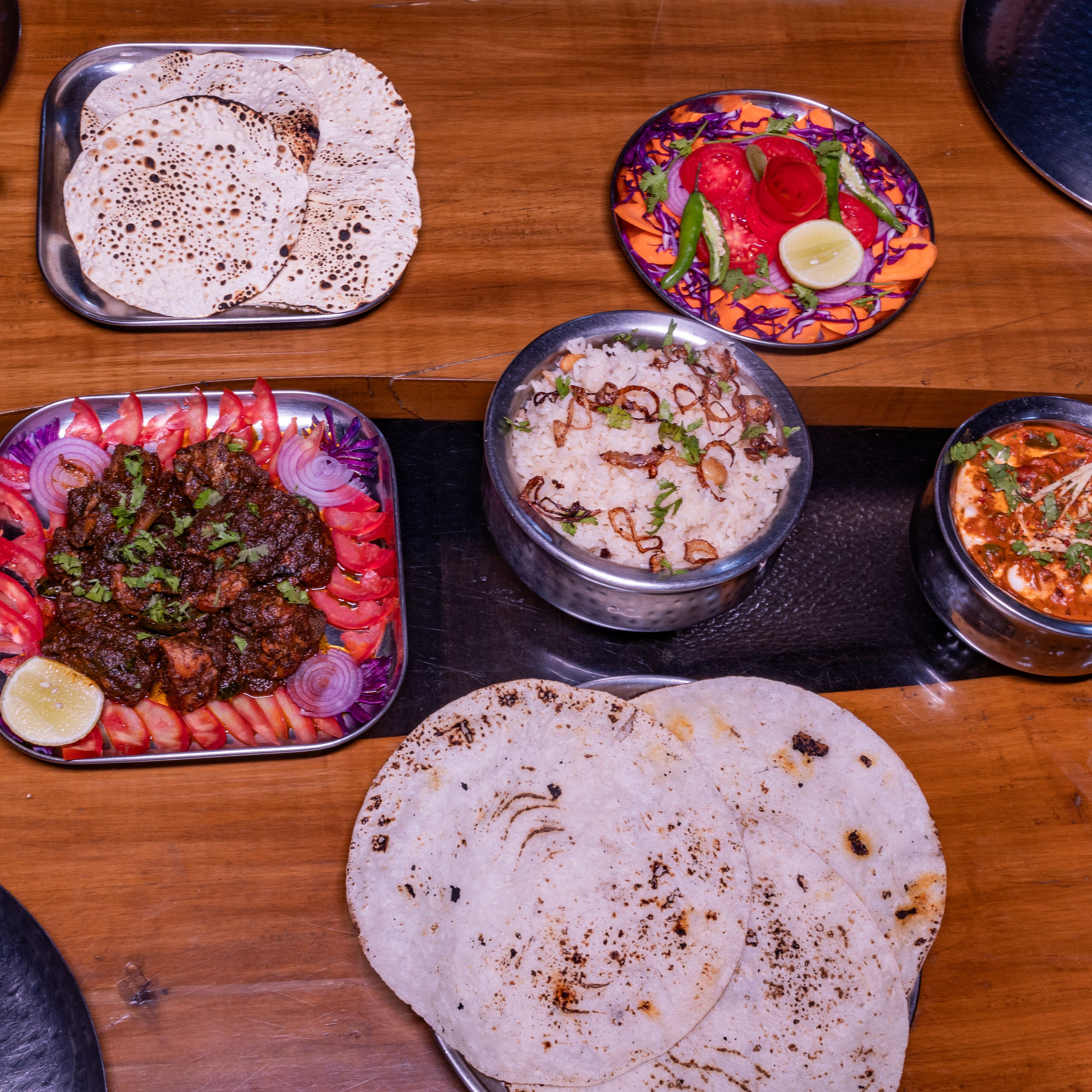 Diversos pratos indianos, incluindo pães achatados, uma salada e um prato com carne, servidos em pratos de metal.