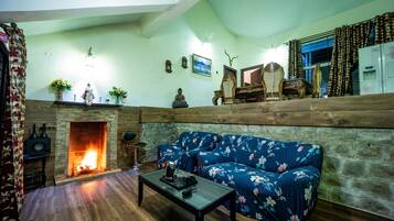 Uma sala de estar aconchegante com lareira, um sofá floral e uma mesa de centro de madeira.