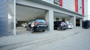 Garagem de estacionamento com vários carros estacionados sob um edifício moderno com detalhes vermelhos.