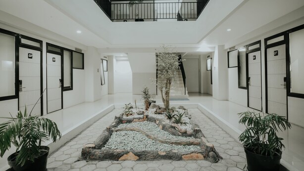 Um hall amplo com um jardim central, uma escadaria e um mezanino.