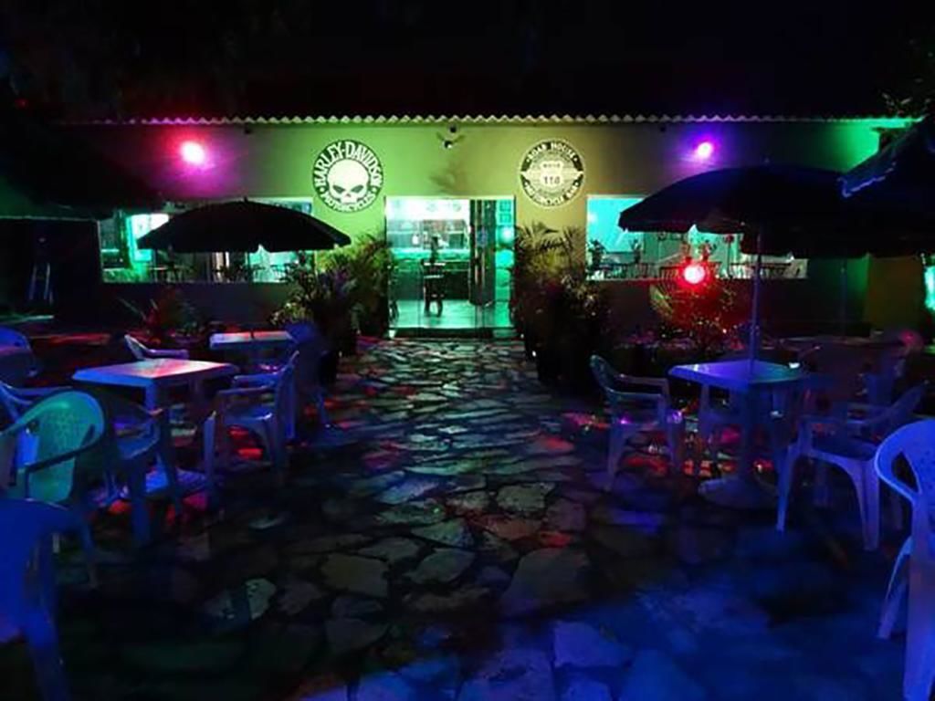 Uma área de pátio externa com mesas e cadeiras, um caminho de pedra e um edifício com letreiros luminosos ao fundo.