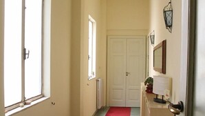 Um corredor estreito com carpete vermelho, uma porta branca no final e um radiador na parede.