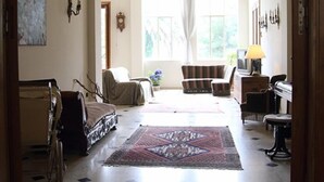Uma sala de estar ampla com uma grande janela, um tapete estampado e um piano.
