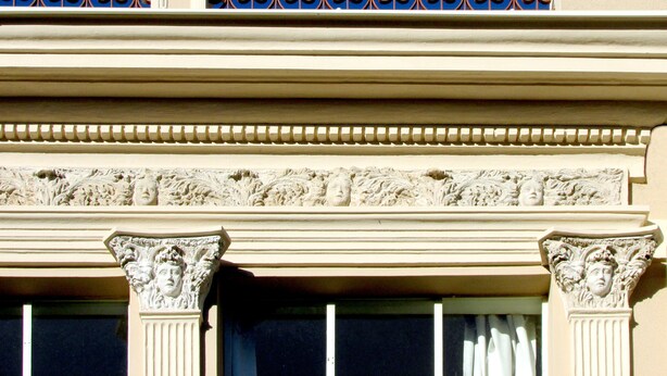 Fachada de edifício com detalhes arquitetônicos ornamentados, incluindo molduras decorativas e uma varanda com grades de ferro forjado.