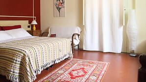 Quarto com cama grande, mesa de cabeceira, luminária, cadeira e janela com cortinas.