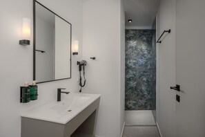 Um banheiro moderno com um lavatório branco, um espelho grande e um chuveiro com um padrão de folhas na parede.