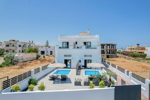Um edifício moderno de dois andares com área de piscina no terraço, com área de estar externa e vista clara do bairro ao redor.