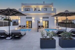 Uma área de piscina no terraço com espreguiçadeiras, guarda-sóis e plantas em vasos.