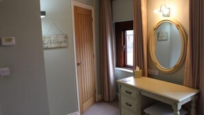 Um quarto com toucador, espelho, mesa de cabeceira, janela com cortinas e porta.
