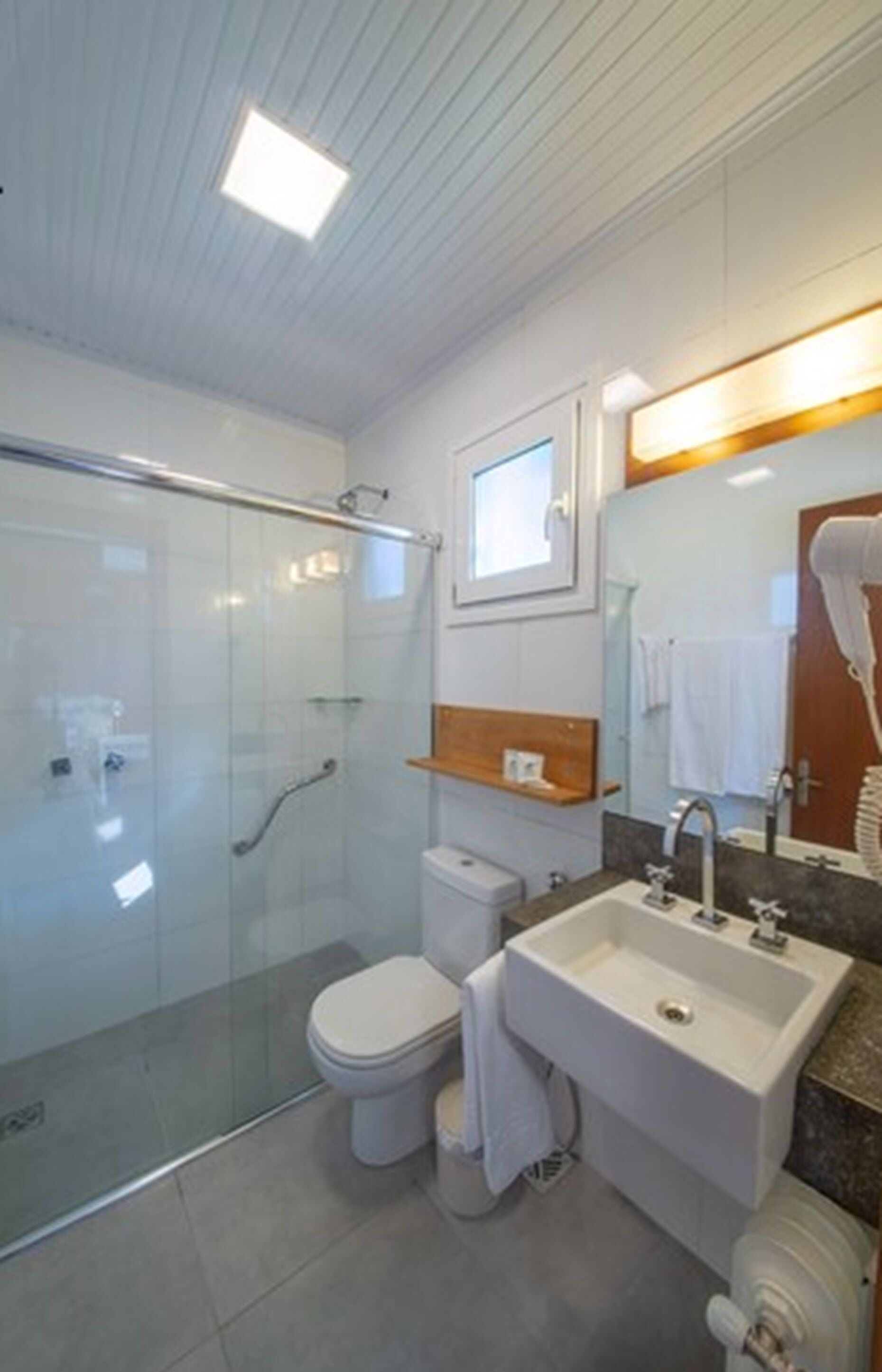 Um banheiro moderno com chuveiro de vidro, vaso sanitário branco, pia com espelho acima e toalha pendurada na parede.