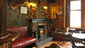 Um quarto aconchegante com parede de pedra, lareira, teto de madeira e uma guitarra pendurada na parede.