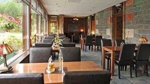 Restaurante com um balcão comprido, cabines e mesas. Há plantas em vasos e vista para o verde lá fora.
