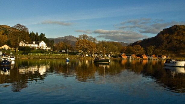 Um lago tranquilo com barcos, uma casa grande e colinas ao redor.
