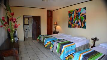 Quarto de hotel com duas camas, uma escrivaninha, uma cadeira, um vaso com flores, um quadro na parede e um ventilador de teto.