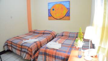 Quarto de hotel com duas camas, um quadro na parede, uma luminária e uma planta no criado-mudo.