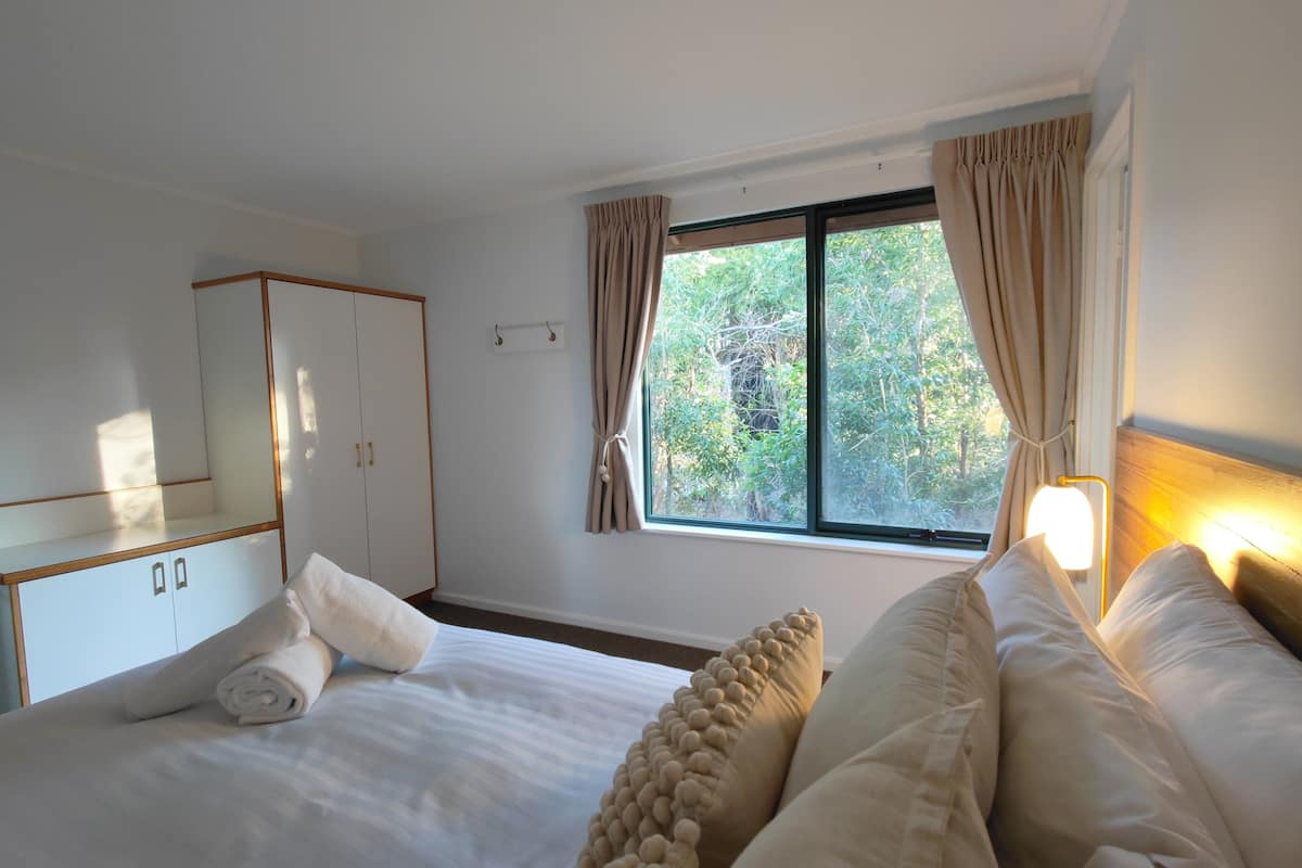 Quarto com cama, guarda-roupa, janela com cortinas e luminária de cabeceira.