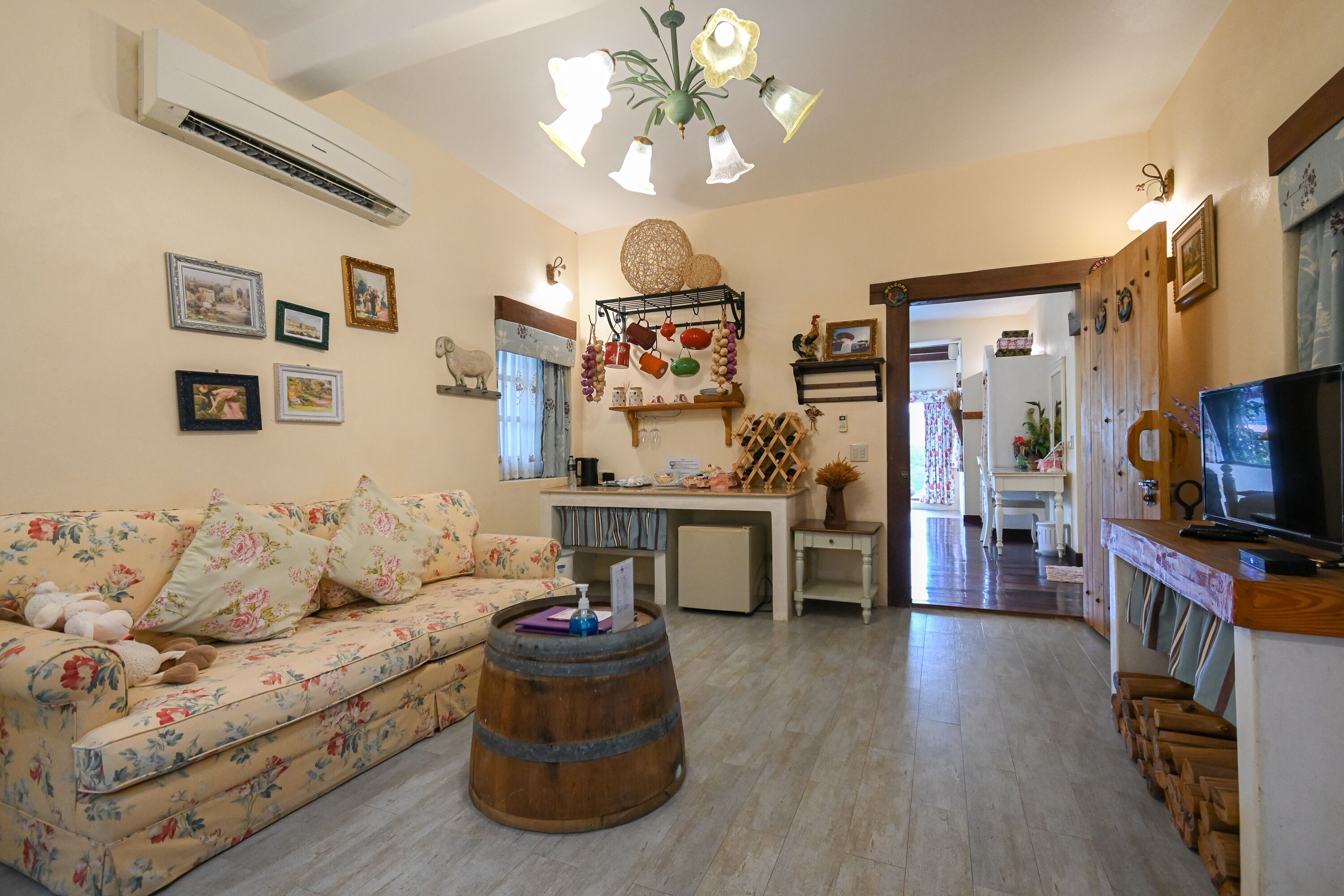 Uma sala de estar com um sofá floral, uma mesa de centro em forma de barril de madeira e uma televisão sobre um suporte de madeira.