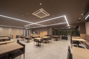 Uma sala de jantar moderna com várias mesas e cadeiras, uma área de cozinha e um espaço de estar com plantas.