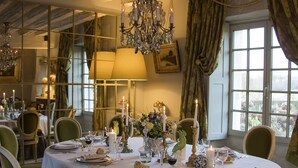 Uma sala de jantar formal com uma mesa redonda posta para uma refeição, velas e um candelabro.