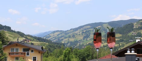 Vista de uma paisagem montanhosa com casas e uma varanda, com dois copos de vinho.