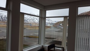 Quarto com amplas janelas que oferecem vista para uma montanha nevada e uma estrada com edifícios ao longe.
