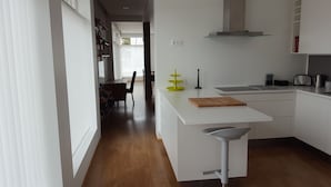 Cozinha moderna com ilha central, área de refeições ao fundo e corredor que leva a outro cômodo.