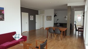 Uma sala ampla com uma mesa de jantar de madeira, duas cadeiras, um sofá vermelho e uma mesa de centro de madeira.