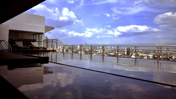Piscina no terraço com vista para a cidade, arquitetura moderna e guarda-corpo de vidro.