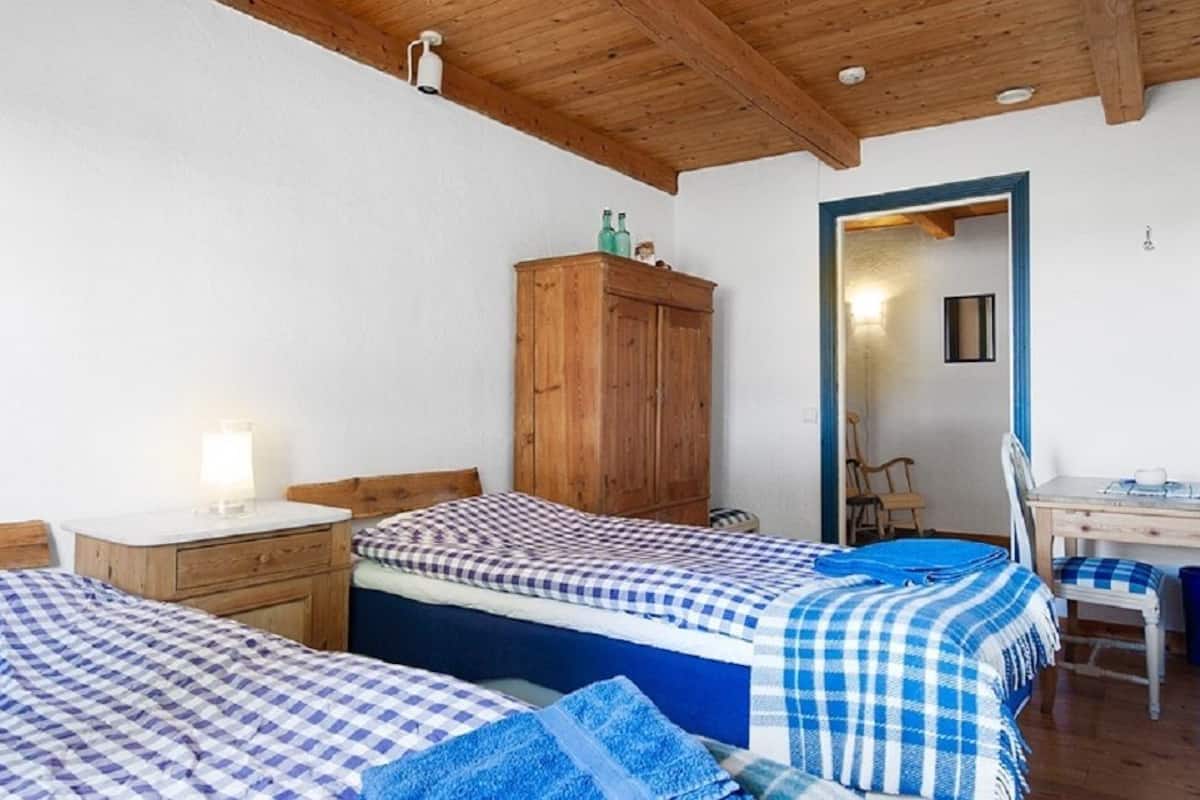 Quarto com duas camas, guarda-roupa de madeira e uma escrivaninha com cadeira.