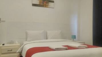 Quarto de hotel com uma cama, mesas de cabeceira brancas, uma pequena mesa e uma obra de arte pendurada na parede.