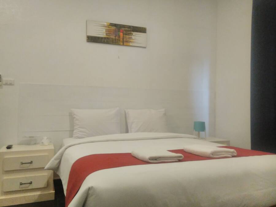 Quarto de hotel com uma cama, mesas de cabeceira brancas, uma pequena mesa e uma obra de arte pendurada na parede.