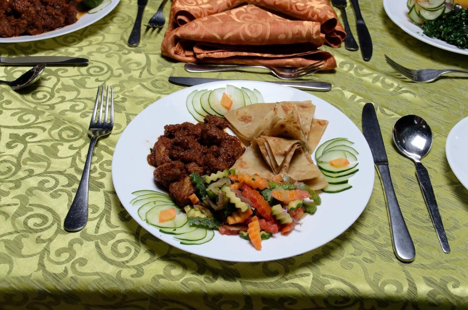 Um prato com comida, um garfo, uma faca e uma colher sobre uma mesa com toalha de mesa estampada.