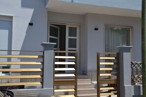 Uma entrada de prédio moderna com portão de madeira, degraus que levam a uma porta e uma janela com cortina.