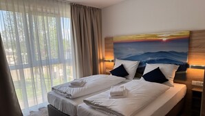 Cama de casal com lençóis brancos, duas almofadas e cabeceira com pintura de pôr do sol.