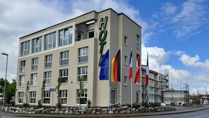 Um hotel moderno com vários bandeiras, incluindo a bandeira da União Europeia, e uma placa indicando um McDonald's próximo.