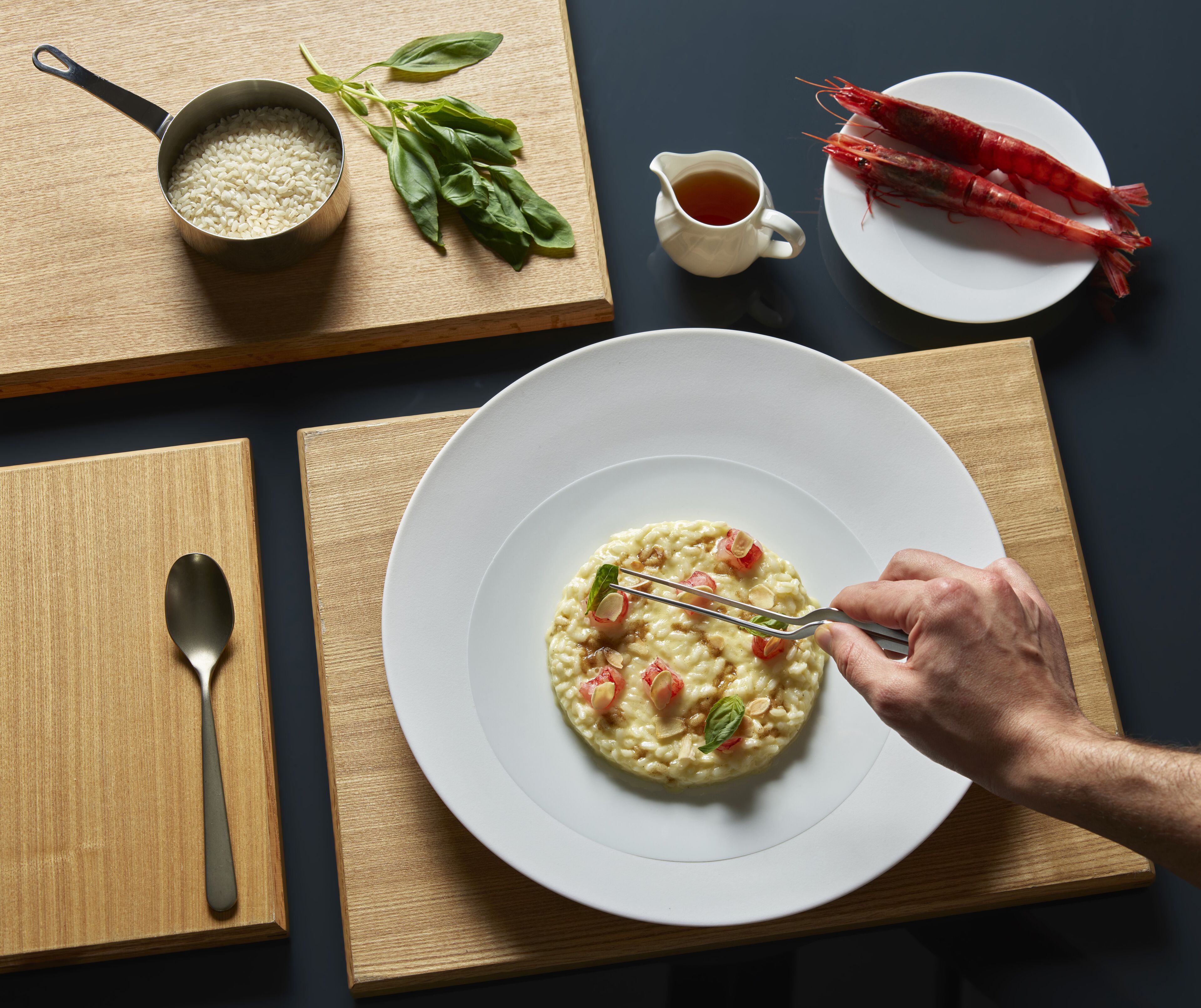 Uma mesa de jantar com um prato de risoto, uma tigela de arroz, uma panela de arroz, um par de pinças, uma colher, uma xícara de chá e dois camarões cozidos em um prato.