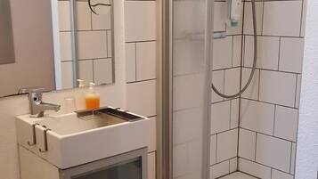 Casa de banho com chuveiro em cabine de vidro, lavatório com espelho e porta-toalhas.