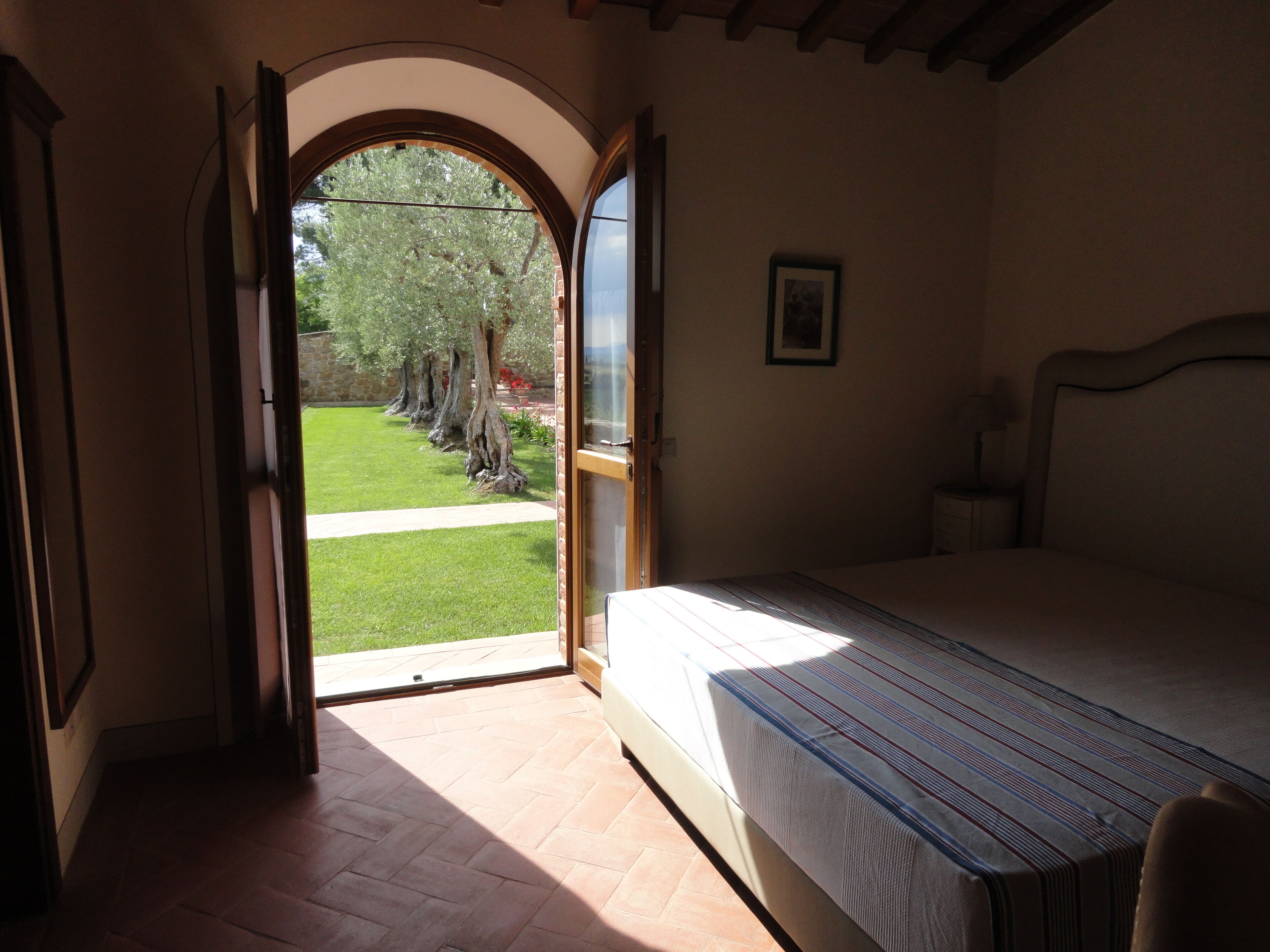 Quarto com uma cama, uma porta que dá para um jardim e um quadro na parede.