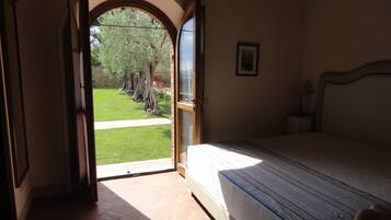 Quarto com uma cama, uma porta que dá para um jardim e um quadro na parede.