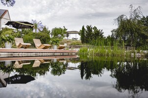 Um ambiente externo tranquilo com um lago espelhado, cadeiras de descanso e plantas em vasos.