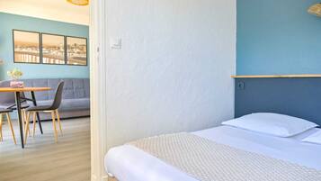 Quarto de hotel com cama, sofá, mesa de jantar e cadeiras, e vista para a paisagem urbana.