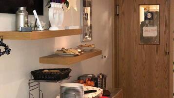 Quarto de hotel com disposição de buffet, incluindo torradeira, pratos e diversas opções de comida em estantes.
