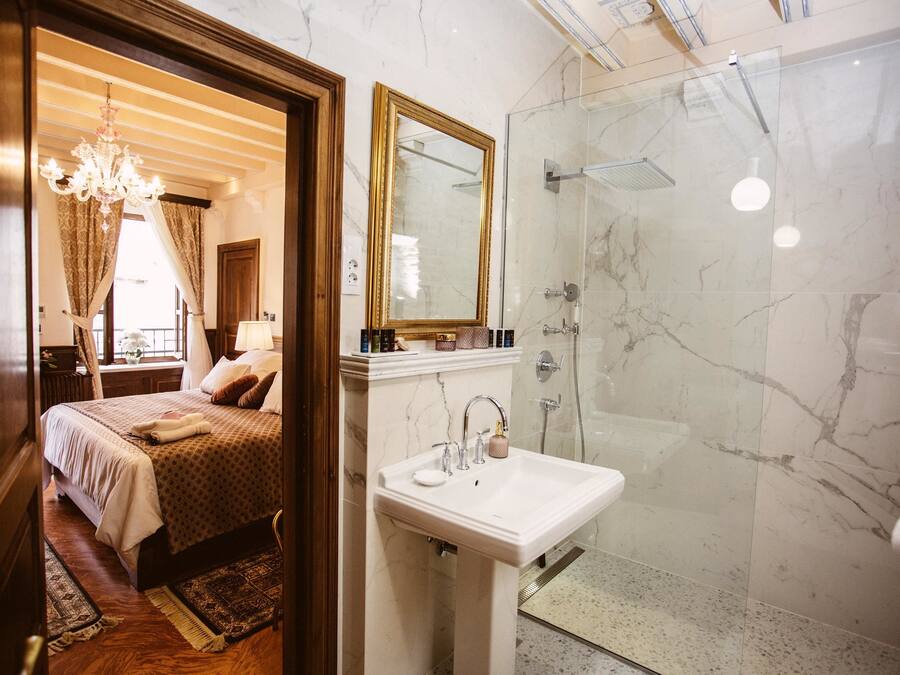 Quarto de hotel com cama, banheiro com pia e espelho, e chuveiro.