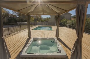 Um deck de madeira com uma banheira de hidromassagem sob um toldo.
