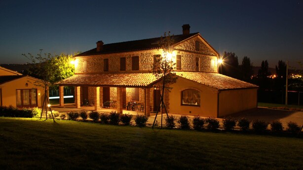 Uma casa de dois andares com telhado ladrilhado e varanda frontal bem iluminada.