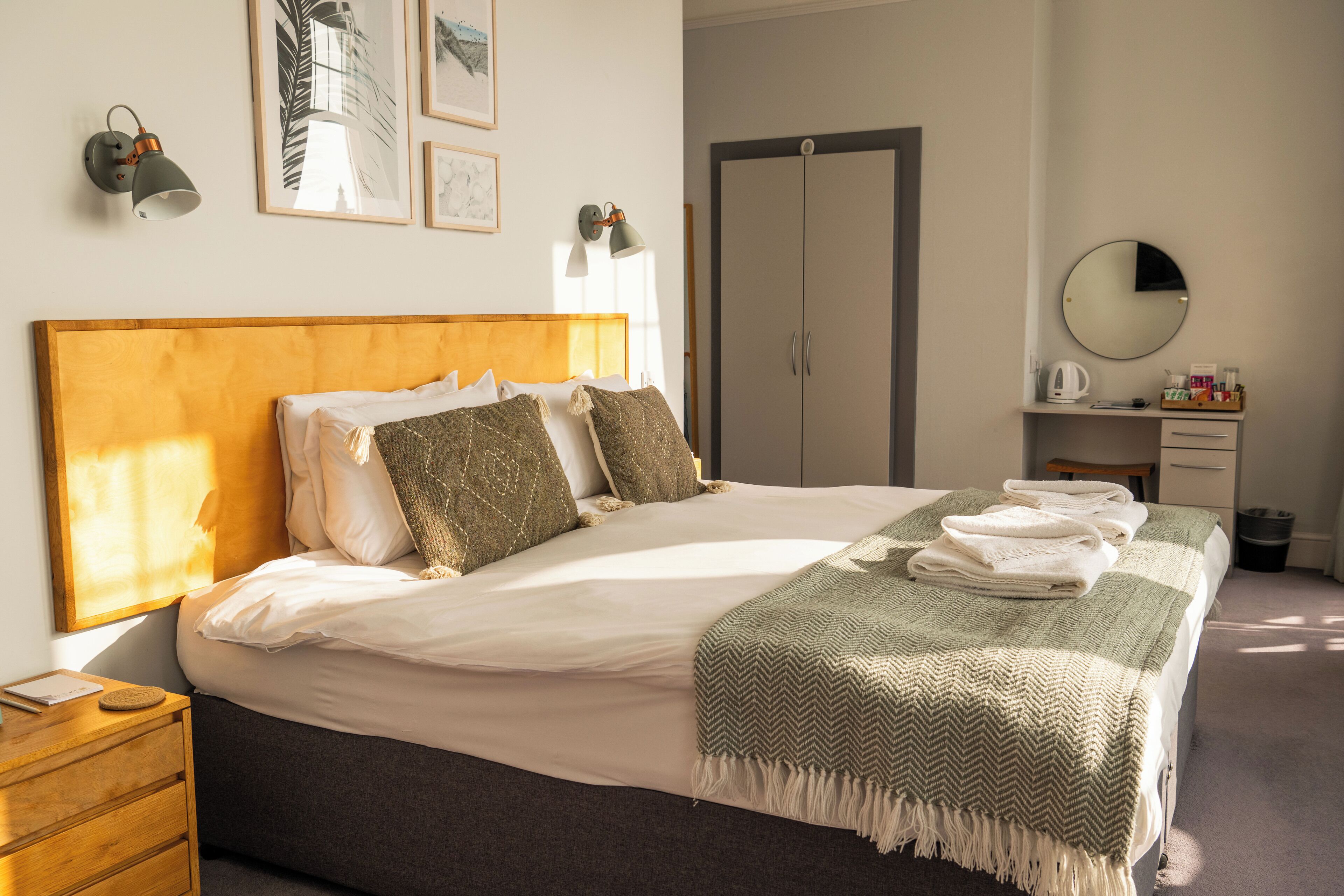 Uma cama bem arrumada com cabeceira de madeira, manta verde e branca e mesa de cabeceira com abajur e um livro.