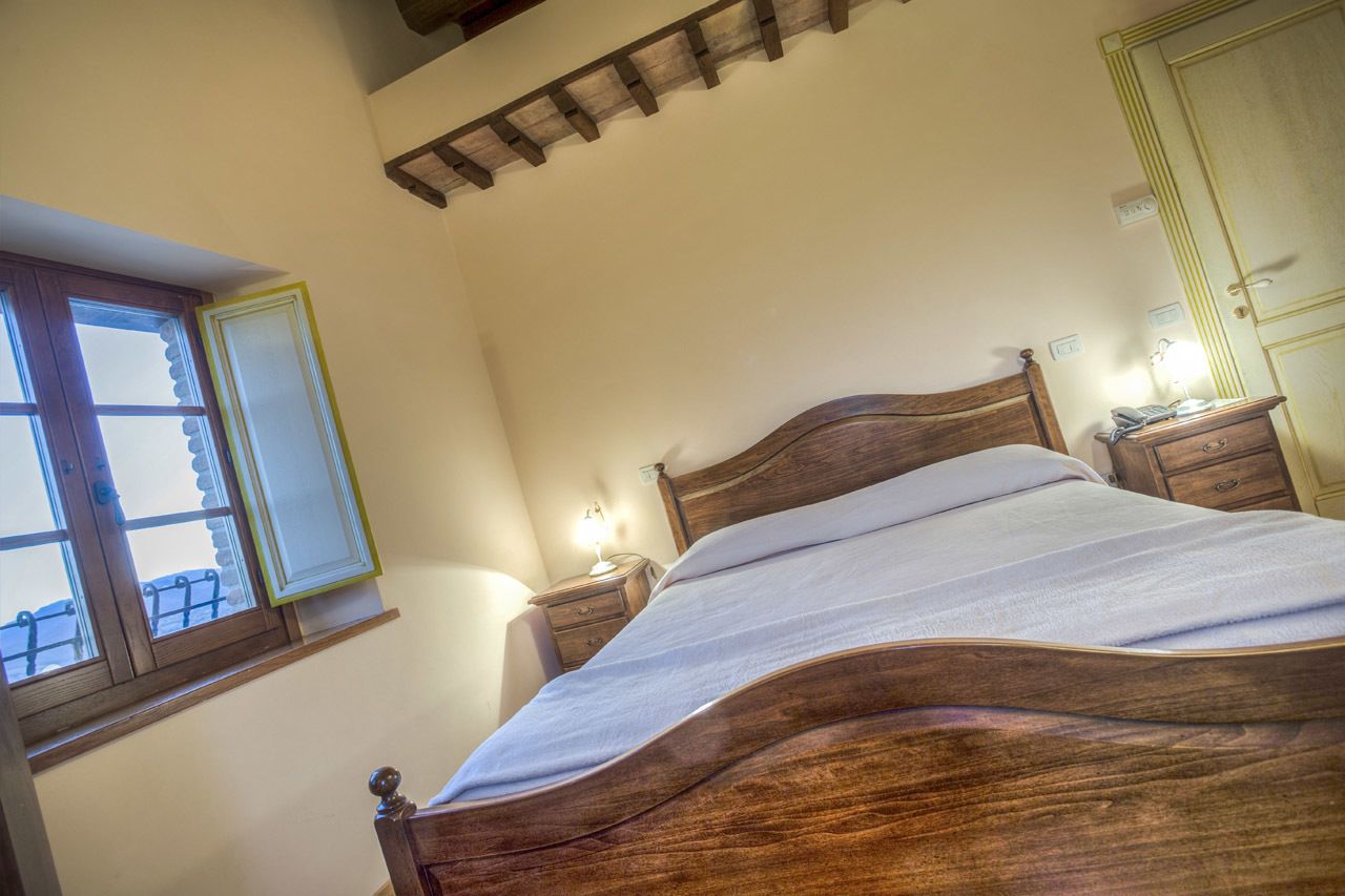 Quarto com cama de madeira, mesa de cabeceira com abajur, janela com vista e guarda-roupa.