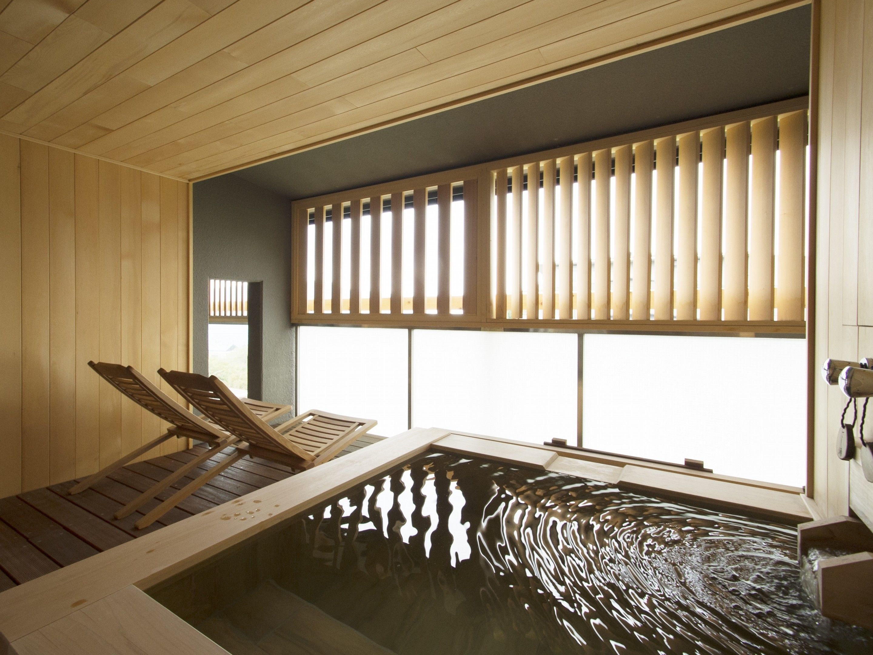 Uma onsen japonesa tradicional com bancos de madeira e uma grande janela com persianas verticais.