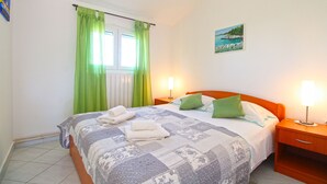 Quarto com cama, cortinas verdes, um quadro e duas luminárias de cabeceira.