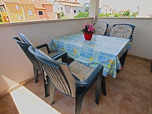 Uma varanda com mesa e cadeiras, um vaso de planta e vista para edifícios.